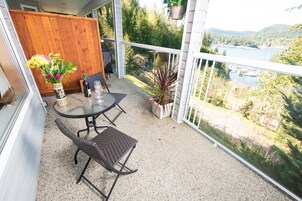 Uma varanda com mesa e cadeiras, um vaso de flores e vista para um lago e uma floresta.