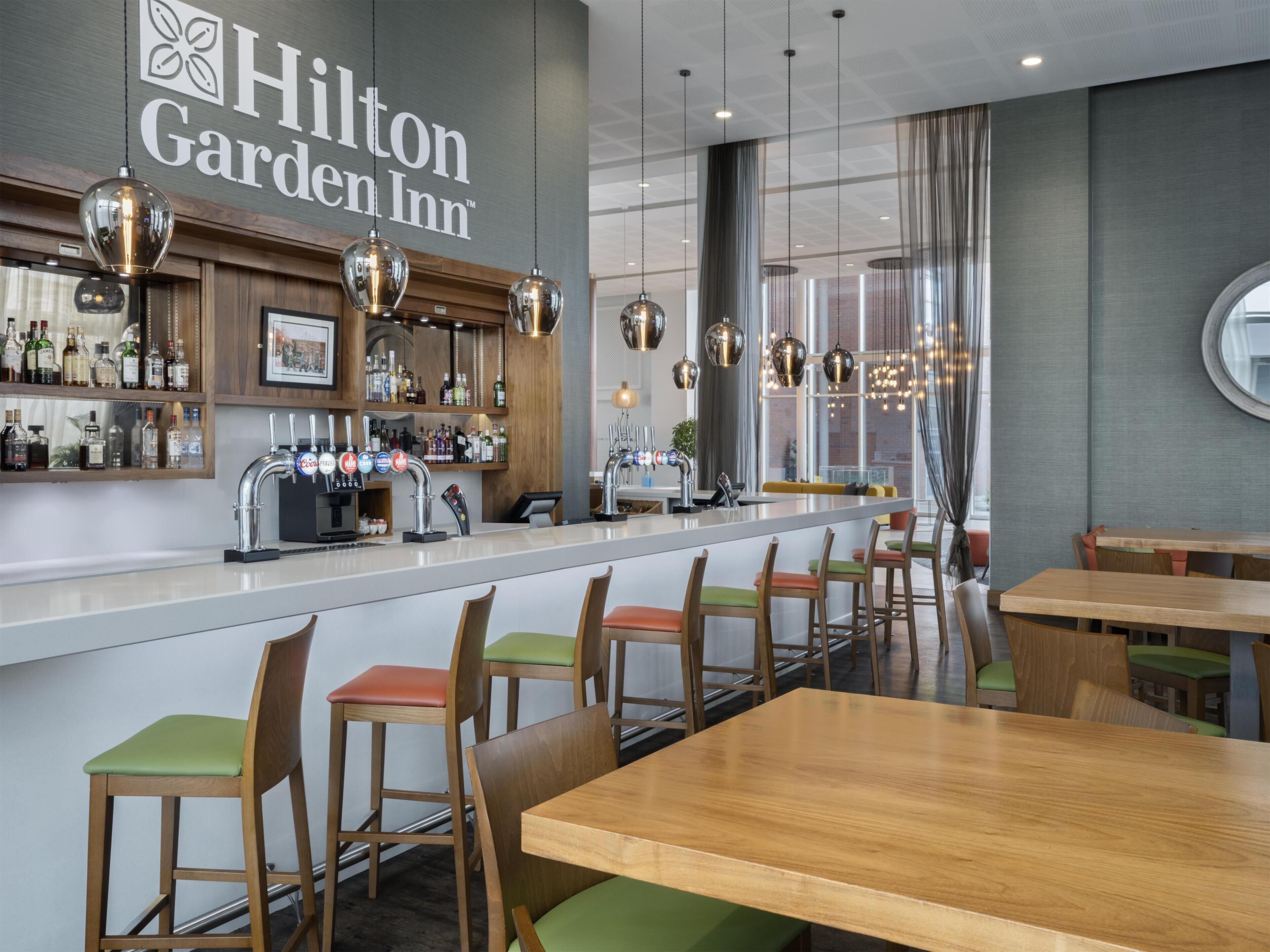 Uma área de bar com minibar, banquetas e um espaço de estar com mesas e cadeiras.