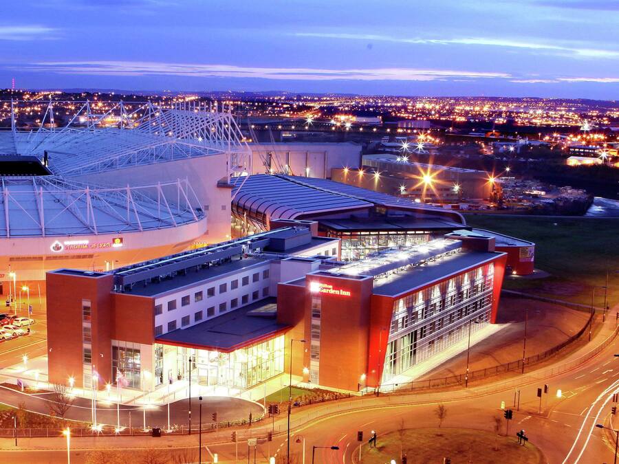 Um estádio com um grande teto curvo e edifícios próximos, com janelas iluminadas e sinalização.