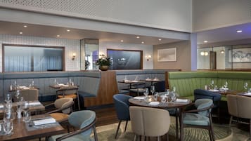 Um restaurante com cabines e mesas, um espelho grande e um arranjo de plantas.