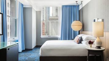 Quarto de hotel com cama, mesa de cabeceira com luminária, janela com cortinas e vista para a cidade.