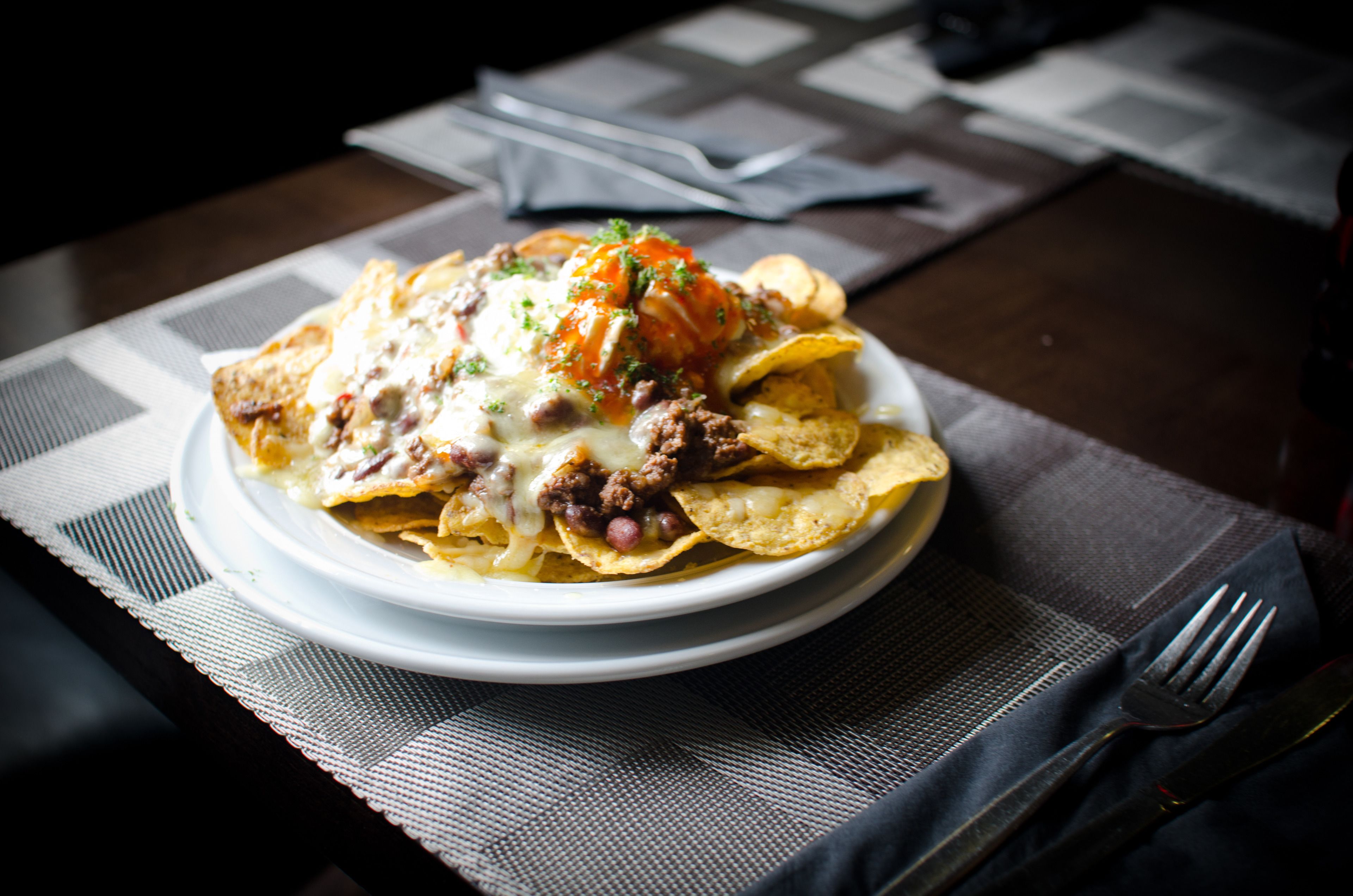 Um prato de nachos com queijo, carne e tomate sobre uma mesa com jogo americano.