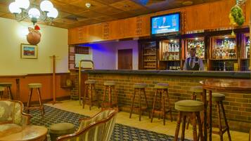 Uma área de bar com móveis de madeira, uma tela de televisão e um bartender.