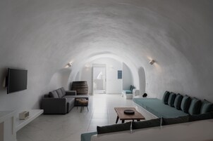Um espaço de estar moderno e aberto, com teto abobadado, TV de tela plana na parede, sofá, mesa de centro e uma pequena mesa lateral.