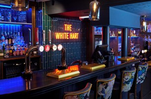 Uma área de bar com um letreiro de neon que diz "The White Hart", uma torneira de cerveja e um caixa registradora.