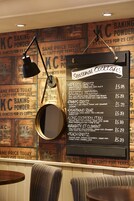 Quadro de menu com cocktails da estação e preços, uma luminária pendente e anúncios antigos de fermento na parede.