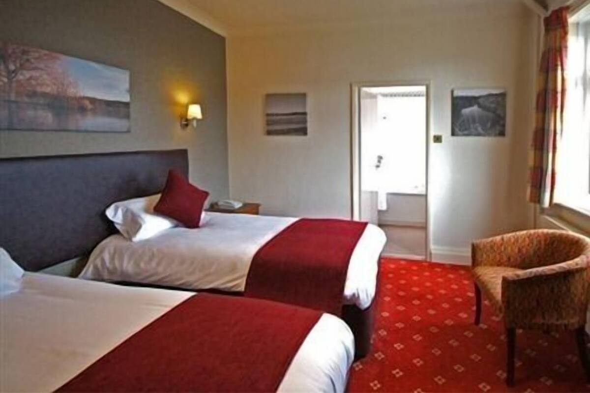 Quarto de hotel com duas camas, uma cadeira e uma porta para o banheiro.