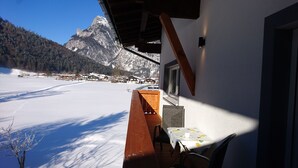 Paisagem coberta de neve com uma montanha ao fundo, um deck de madeira e uma mesa com cadeiras.