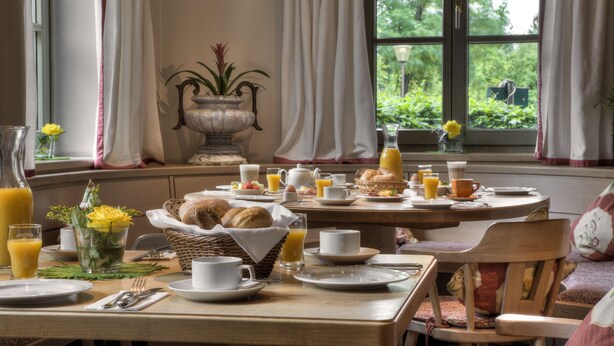 Mesa posta para dois com pão, pastelaria e bebidas.