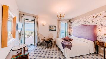 Quarto de hotel com cama, mesa e cadeiras, um candelabro e vista pela janela.