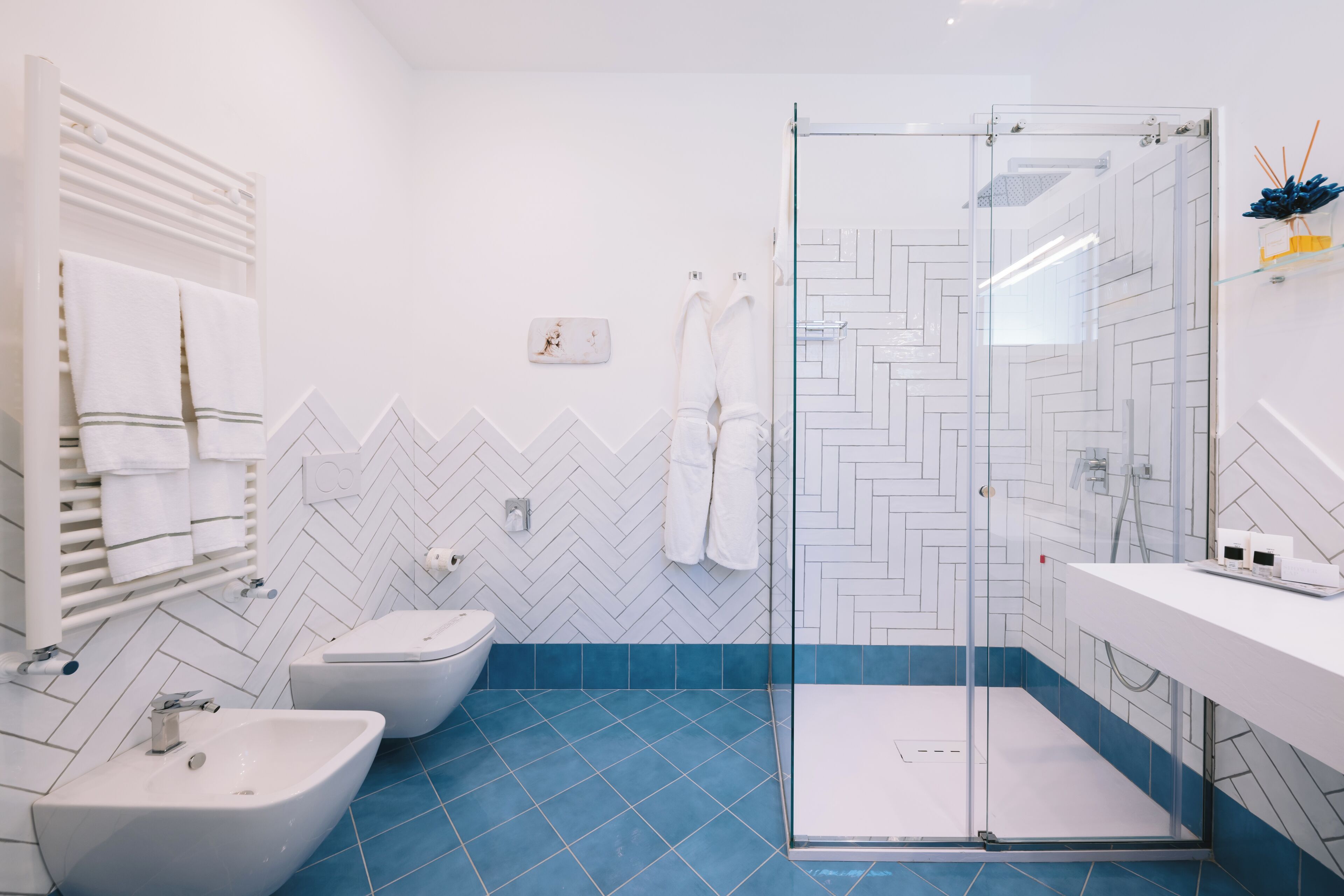 Uma casa de banho moderna com padrão de mosaico em padrão losango, cabine de duche em vidro e lavatório branco.