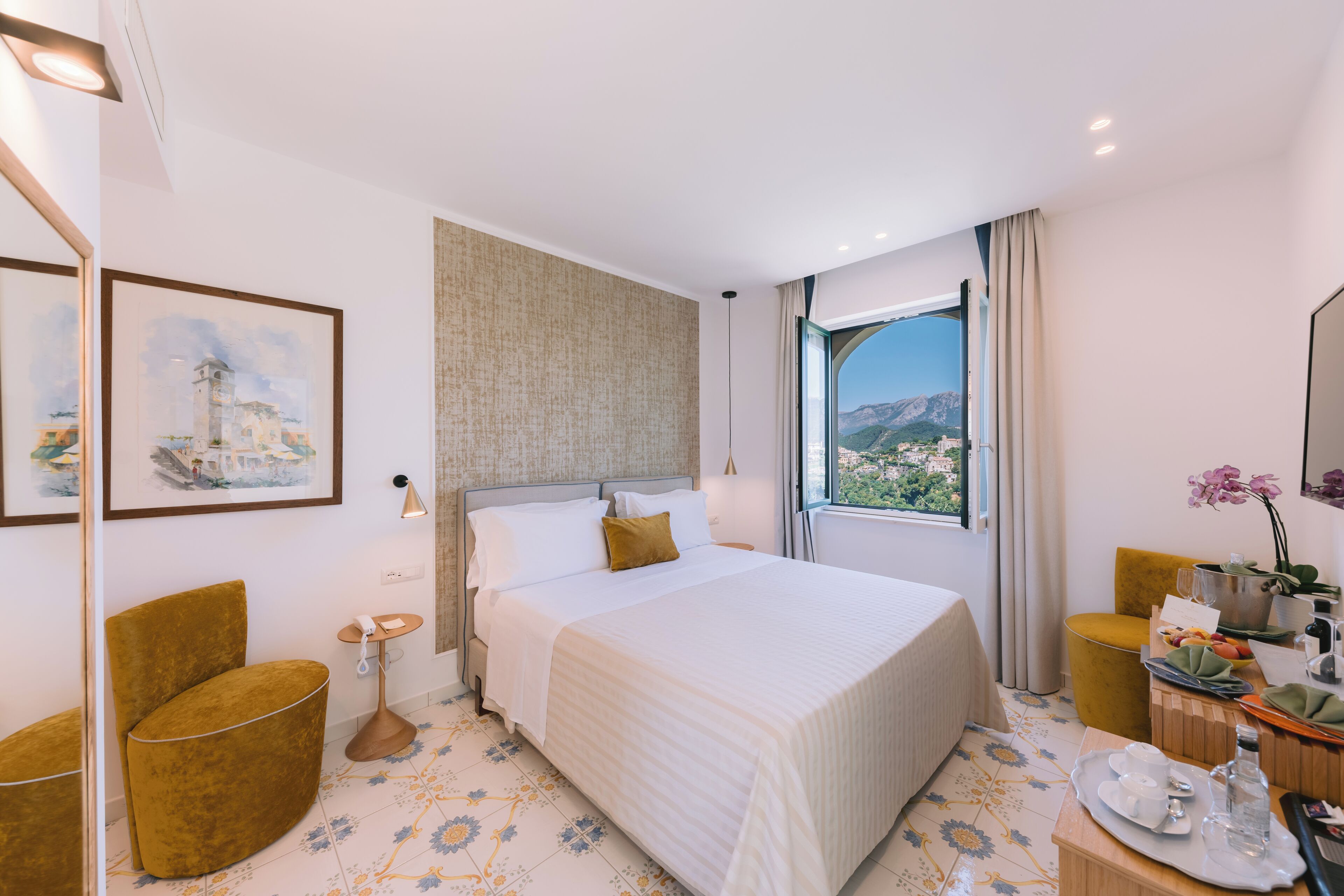 Quarto de hotel moderno com uma cama grande, vista da cidade, uma mesinha com comodidades e um espaço de estar aconchegante.