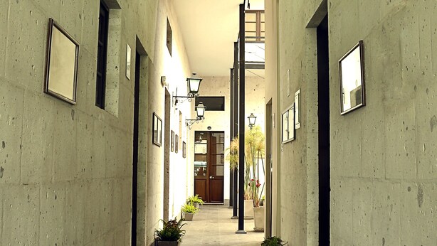 Um corredor com piso de azulejos, quadros nas paredes e plantas em vasos.