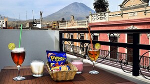 Uma varanda com vista para uma montanha, uma cesta de vime com lanches e duas bebidas com canudos.