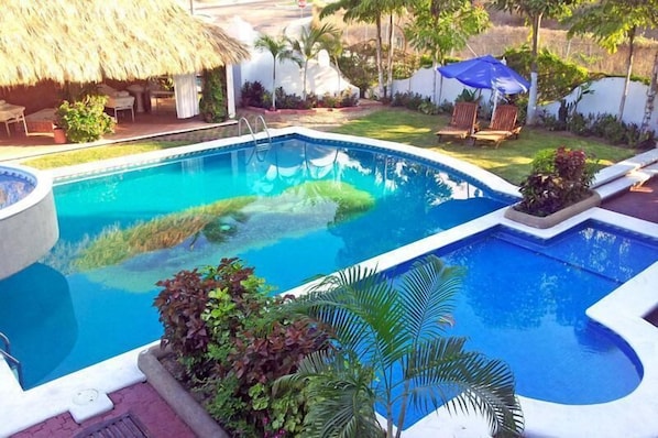 Uma piscina com estrutura de telhado de palha, rodeada por espreguiçadeiras e guarda-sóis.
