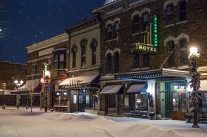 Um edifício histórico com a placa 'Black Hawk Hotel', um 'Sushi Bar & Deli' na rua e neve no chão.