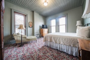 Um quarto com carpete floral, uma cama, uma poltrona, cômoda e televisão.