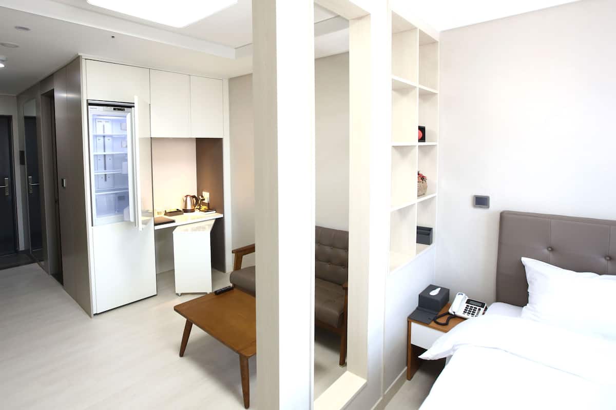 Quarto de hotel moderno com cozinha compacta, um sofá, uma cama e uma mesinha de cabeceira com telefone.