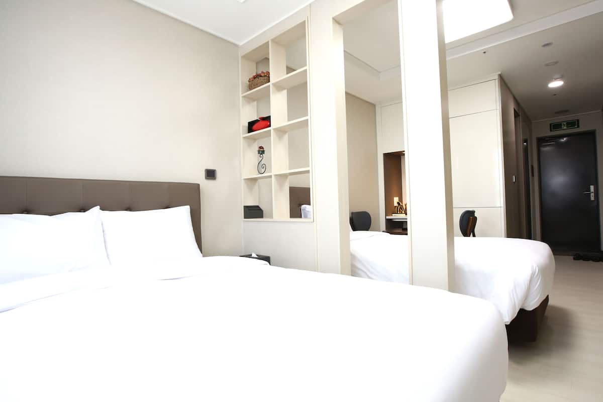 Quarto de hotel com duas camas, um espelho grande e uma estante embutida com objetos decorativos.