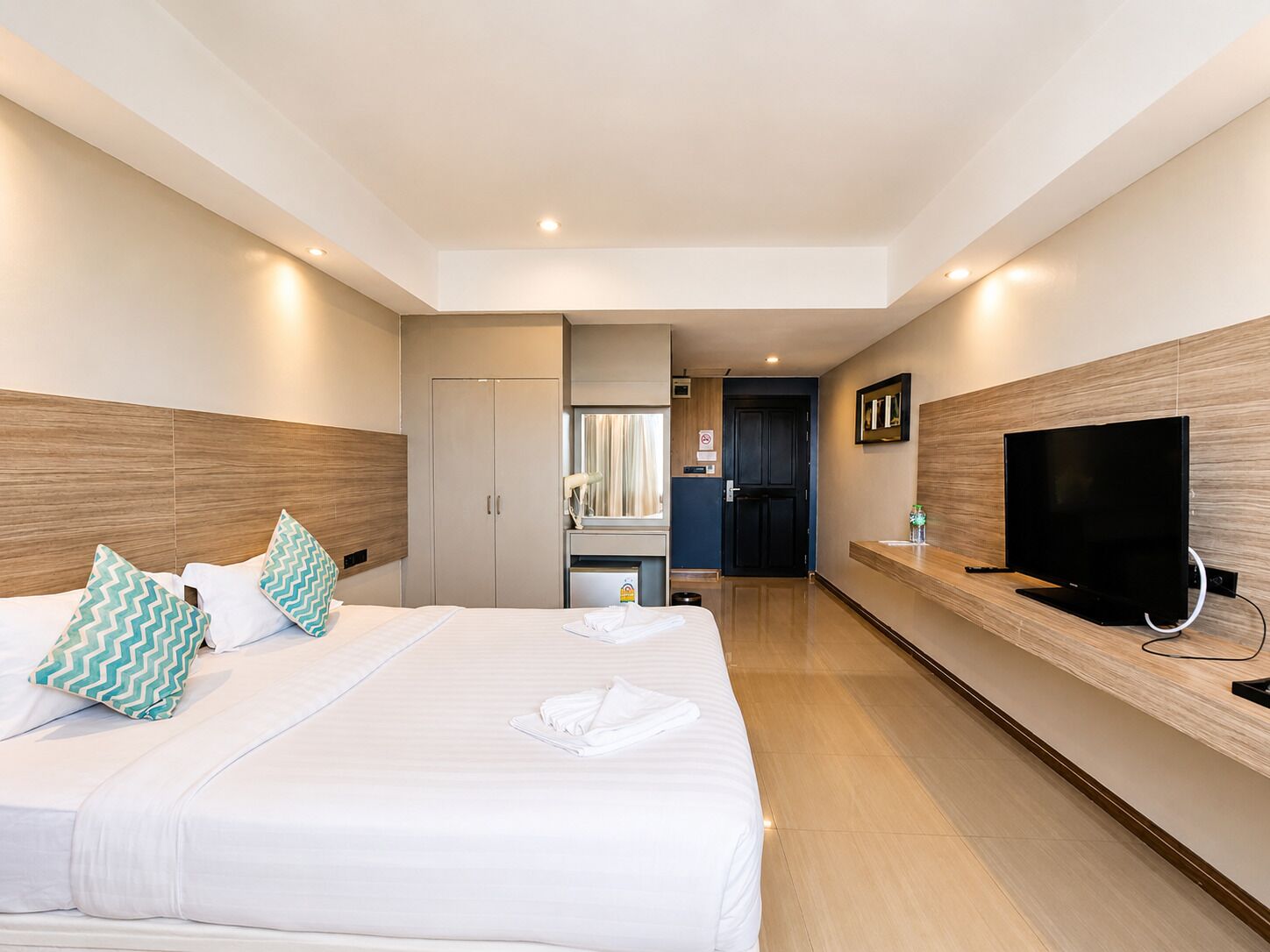 Quarto de hotel com uma cama, televisão, escrivaninha e espelho.