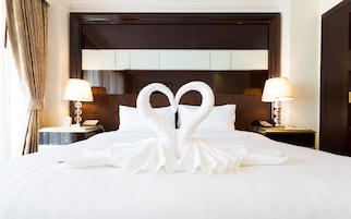 Quarto de hotel com cama, duas mesas de cabeceira, luminárias e um cisne decorativo feito de toalhas.