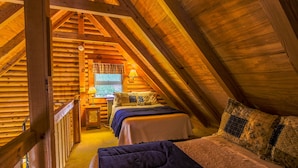 Um quarto de sótão aconchegante com teto inclinado de madeira, uma cama com manta azul e uma janela com cortinas.