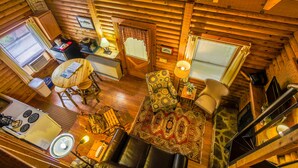 Interior acolhedor de uma cabana de madeira, com sala de jantar, cozinha e sala de estar com lareira.