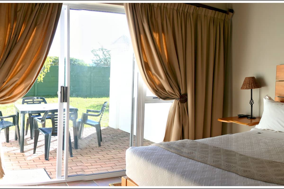 Quarto de hotel com cama, mesa de cabeceira, luminária, mesa e cadeiras, e vista para o exterior.