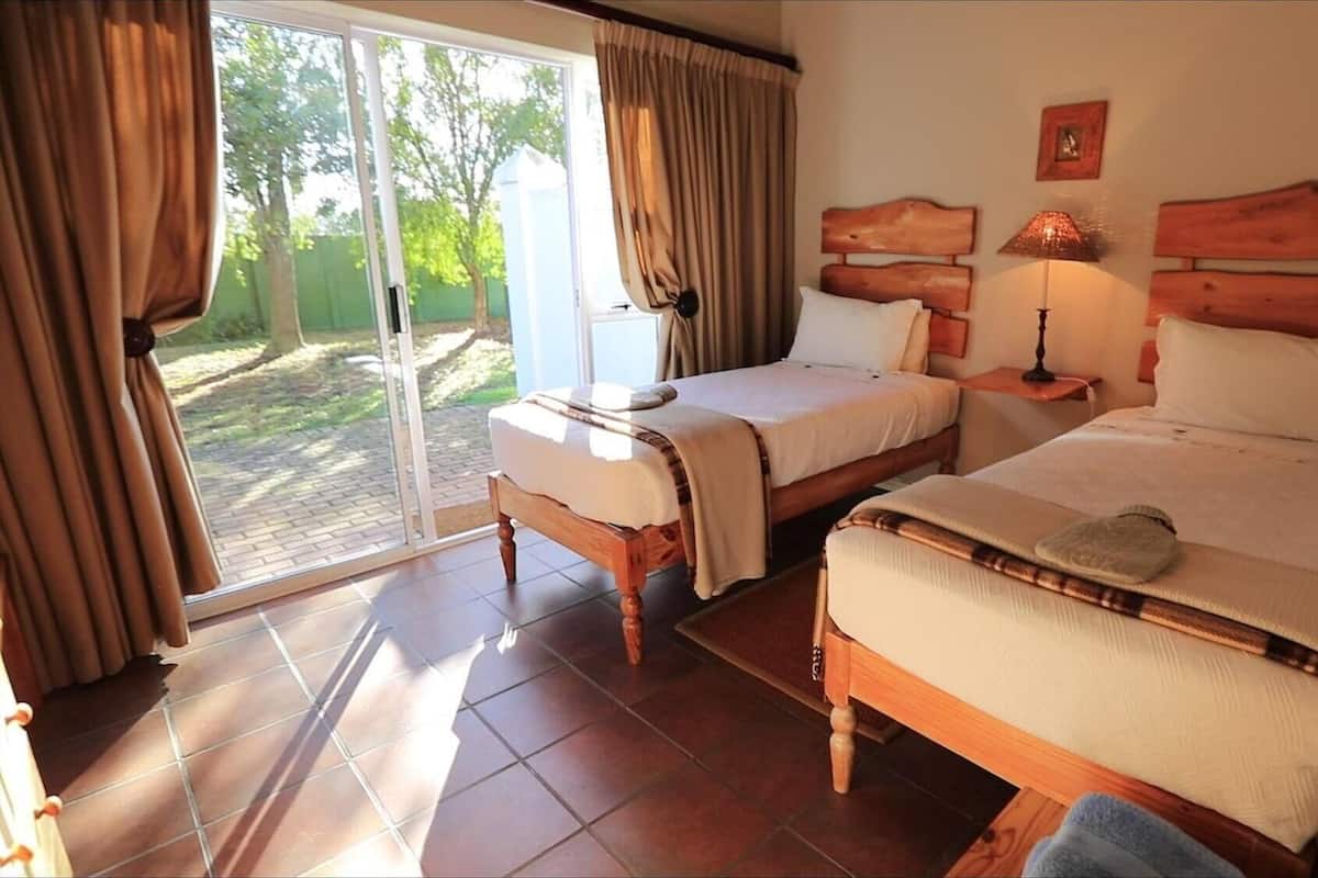 Quarto com duas camas, porta de vidro deslizante para um jardim e uma pequena mesa com abajur.