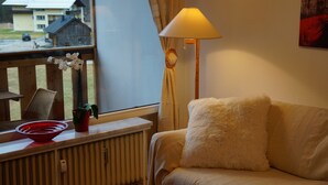 Um quarto aconchegante com um sofá, uma luminária, uma janela com vista para casas e uma tigela vermelha no parapeito.