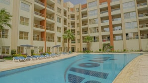 Um hotel com vários andares, piscina, espreguiçadeiras e palmeiras.