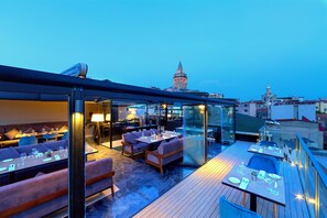 Um restaurante no terraço com mesas ao ar livre, vista para uma torre e área de piscina.