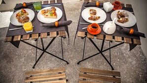 Duas mesas de madeira com itens de café da manhã, incluindo croissants e frutas, e uma bebida verde.