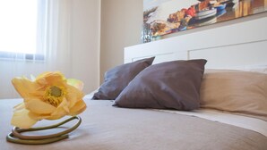 Uma cama com uma única flor amarela grande em um vaso, duas almofadas e um quadro na parede.