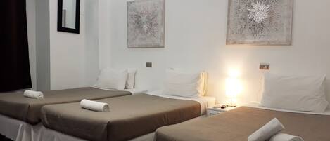 Quarto de hotel com duas camas individuais, cada uma com colcha marrom e almofadas brancas. Existem duas obras de arte na parede representando desenhos florais abstratos. Uma pequena mesa de cabeceira com luminária e tomada elétrica está visível no lado direito do quarto.