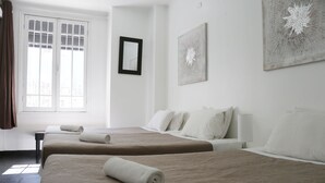 Quarto de hotel com duas camas, uma janela com cortinas e obras de arte nas paredes.
