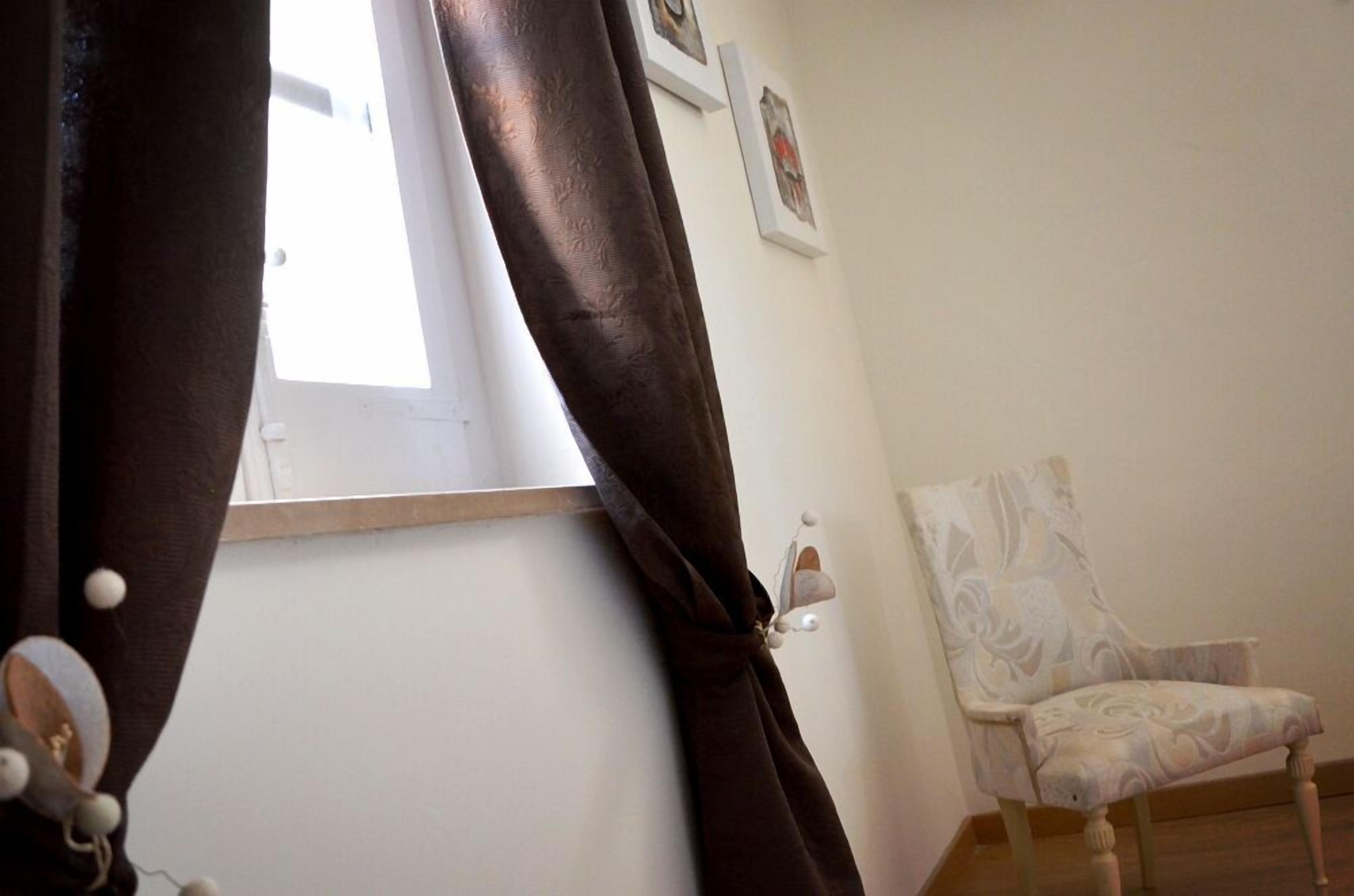 Um quarto com janela, uma cadeira e um quadro na parede.
