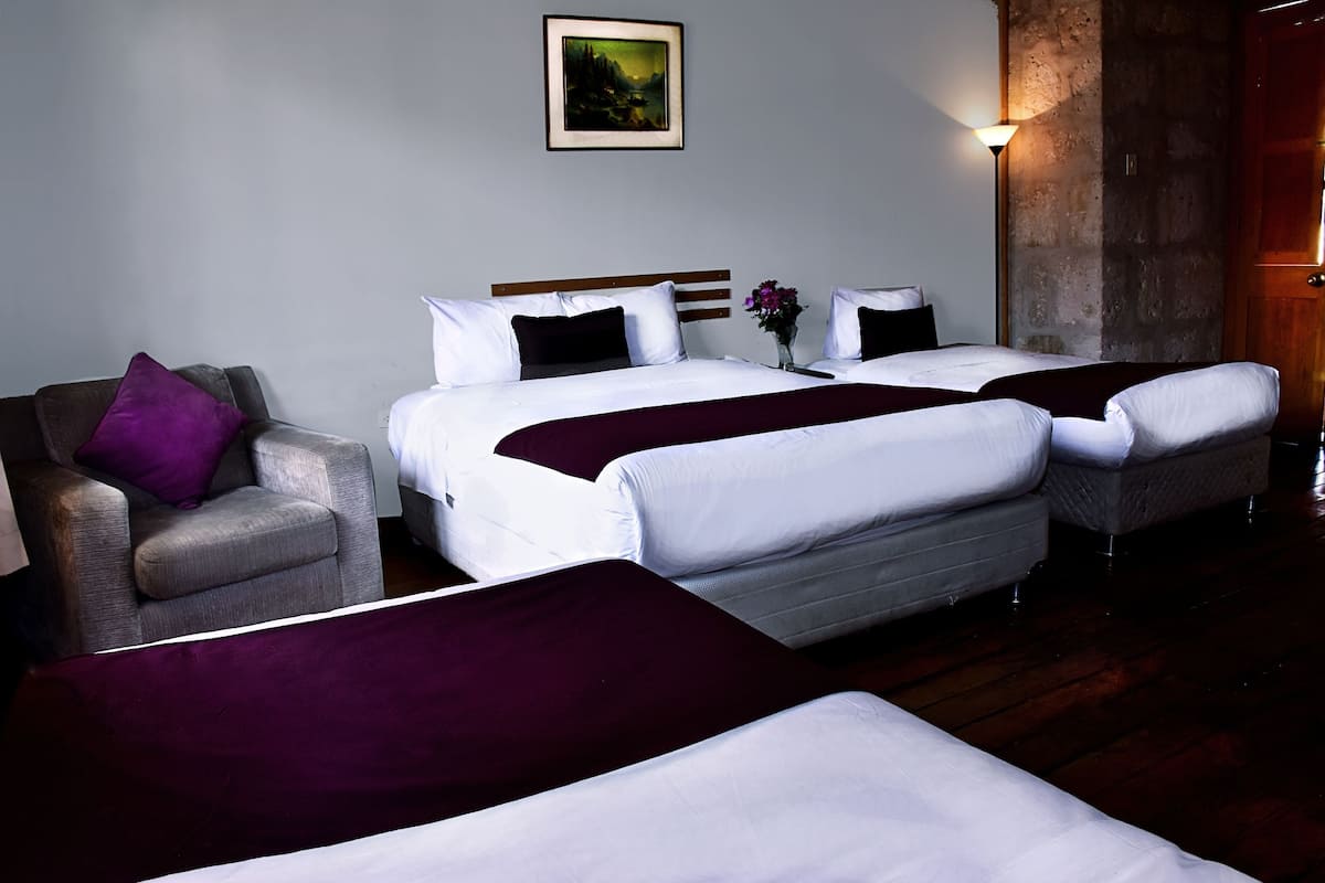Quarto de hotel com duas camas, um sofá e uma mesa de cabeceira com um vaso de flores.