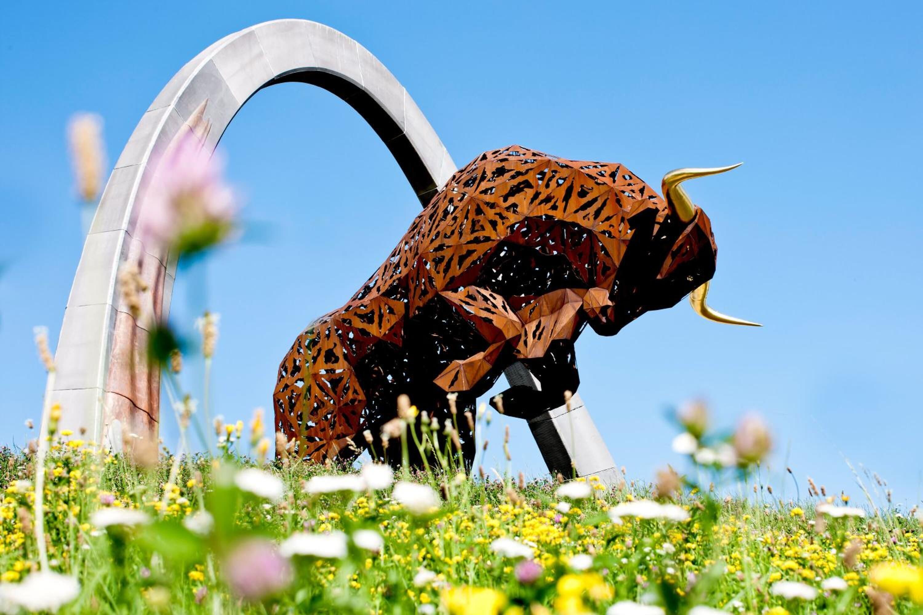 Escultura de touro em um campo sob um céu azul límpido.