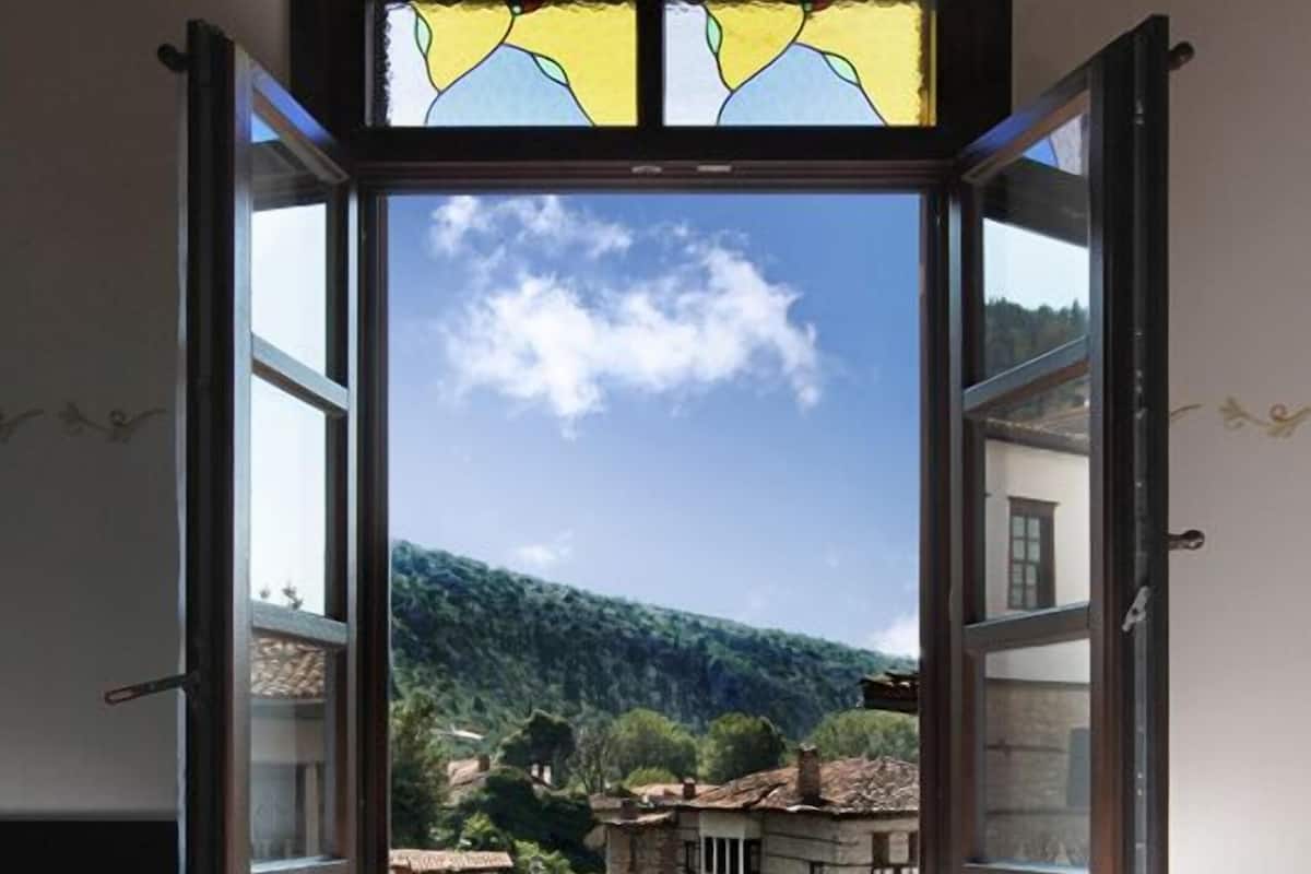 Cama com vista para uma paisagem montanhosa através de uma janela aberta.