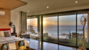 Quarto com uma cama grande, vista para o oceano e varanda com mobiliário de exterior.