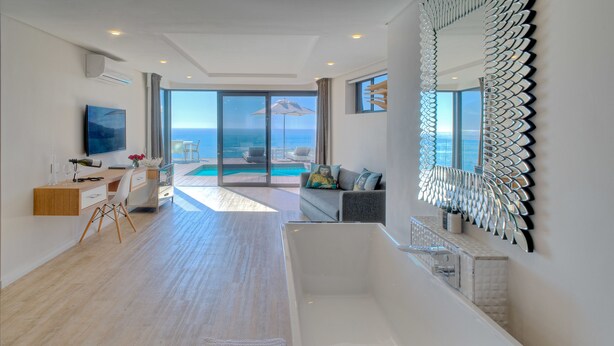 Uma casa de banho moderna com uma banheira grande, uma toucador com espelho e vista para o oceano através de grandes portas de correr.