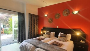 Quarto bem iluminado com uma cama grande, mesa de cabeceira e vista para o exterior através de uma porta deslizante.