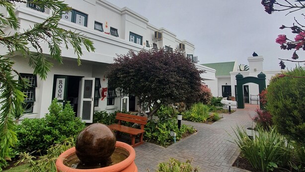 Um edifício com área de jardim, incluindo um caminho, um banco e um elemento aquático.