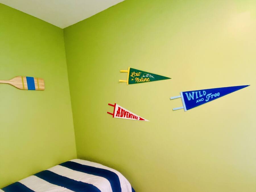 Quarto com cama, parede verde e três bandeirinhas.