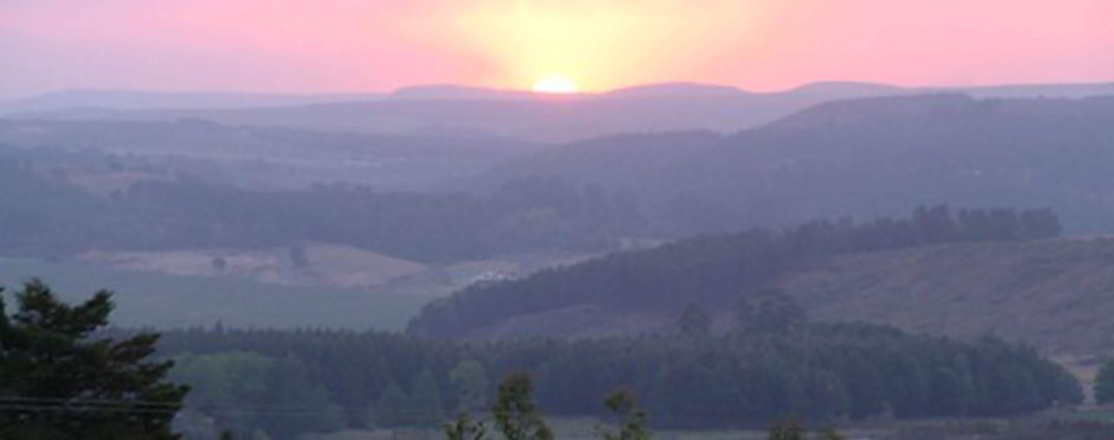 Paisagem com o sol se pondo atrás das colinas.