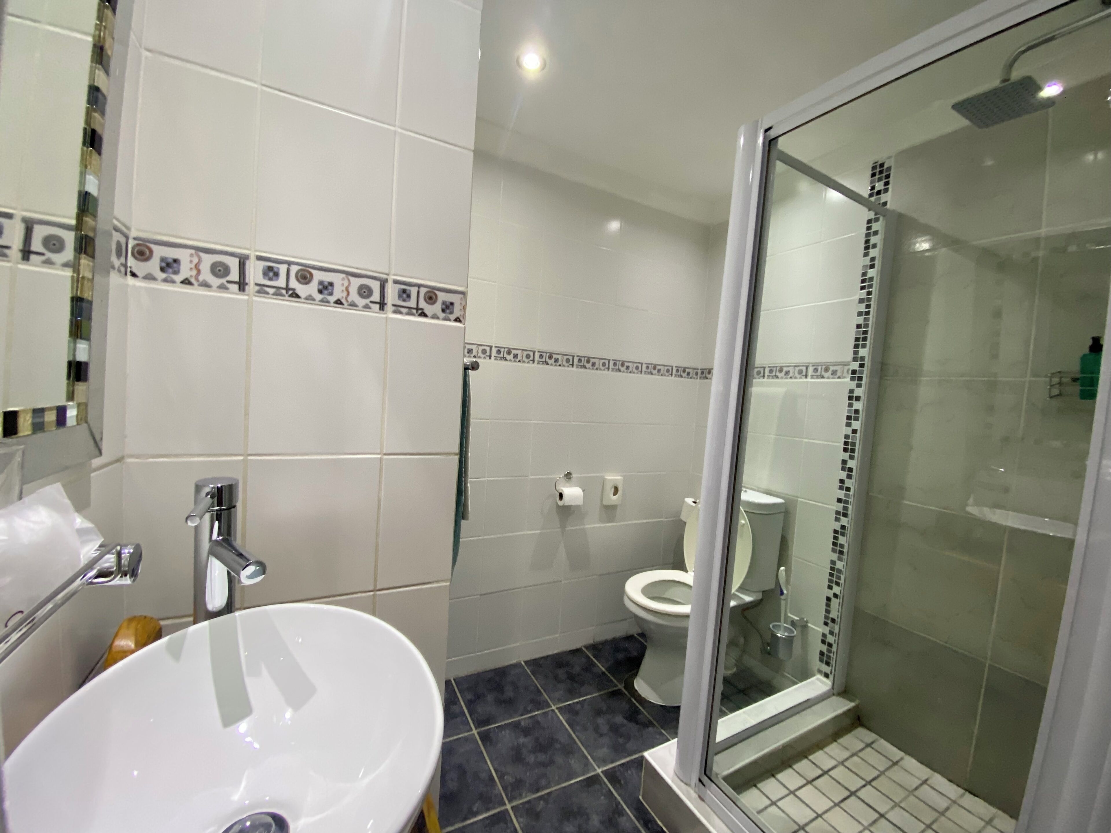 Casa de banho com lavatório branco, sanita e área de duche com divisória de vidro.