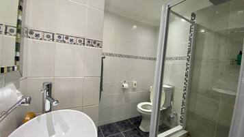 Casa de banho com lavatório branco, sanita e área de duche com divisória de vidro.