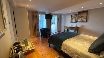 Quarto de hotel com cama, escrivaninha, cadeira, máquina de café e televisão.