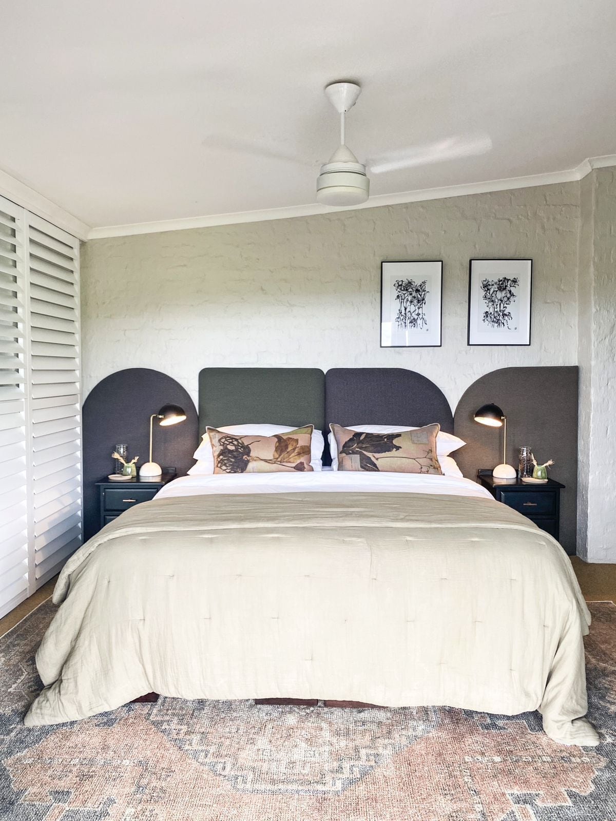 Quarto com cama, duas mesas de cabeceira, um ventilador de teto e duas fotografias emolduradas na parede.